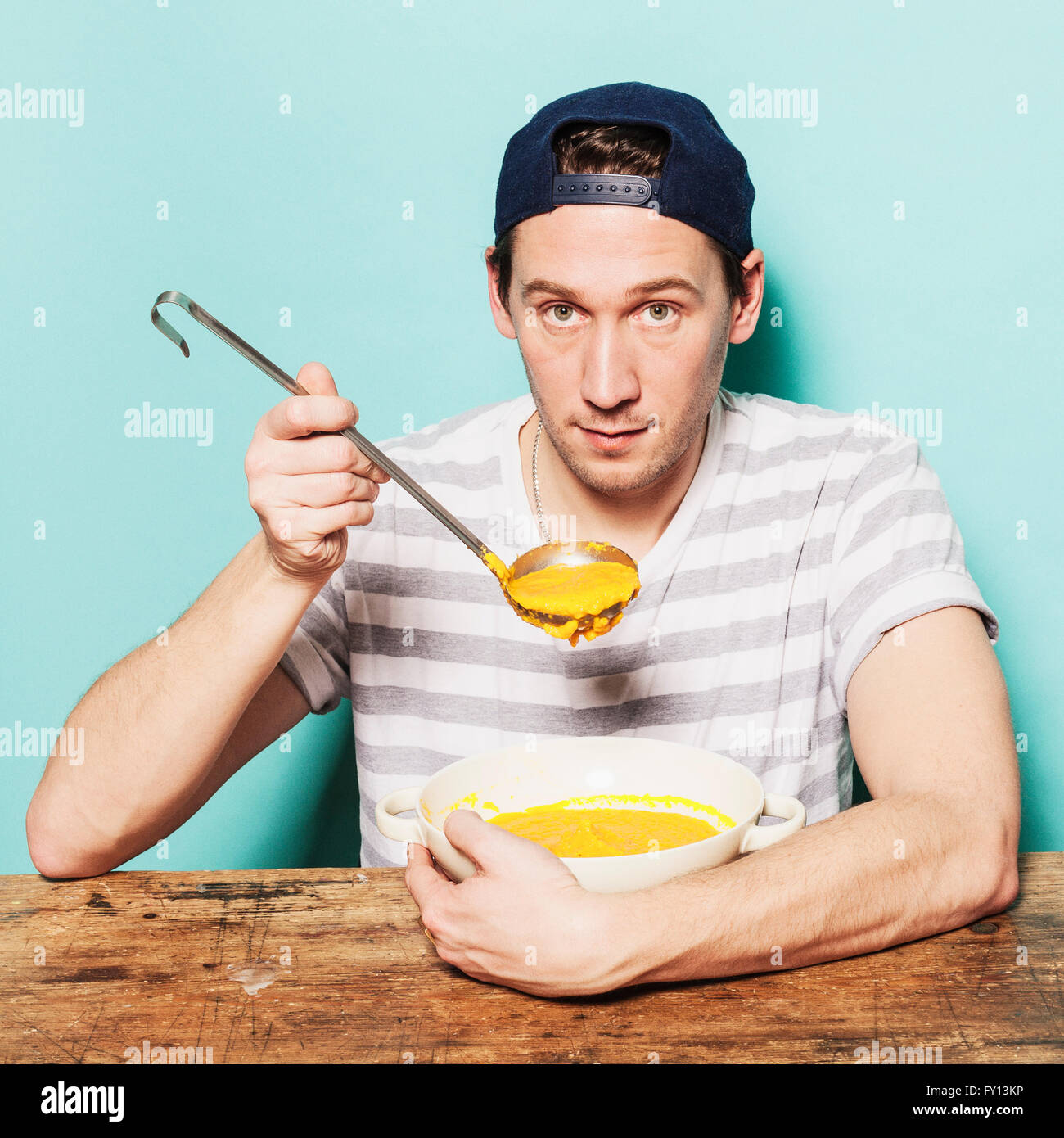 Portrait of confident man having pumpkin soup at table against blue ...