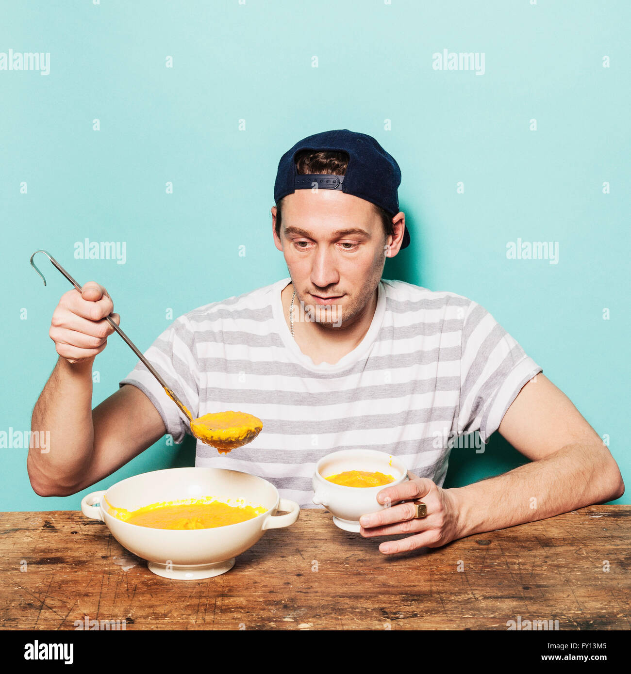 Mid adult man serving pumpkin soup in bowl at table against blue ...