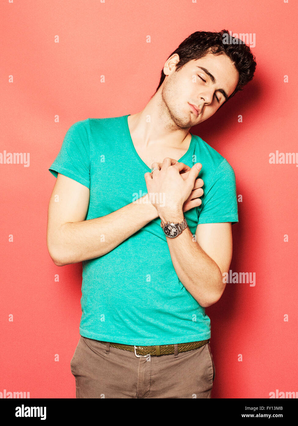 Tired young man sleeping with hands on chest against red background ...