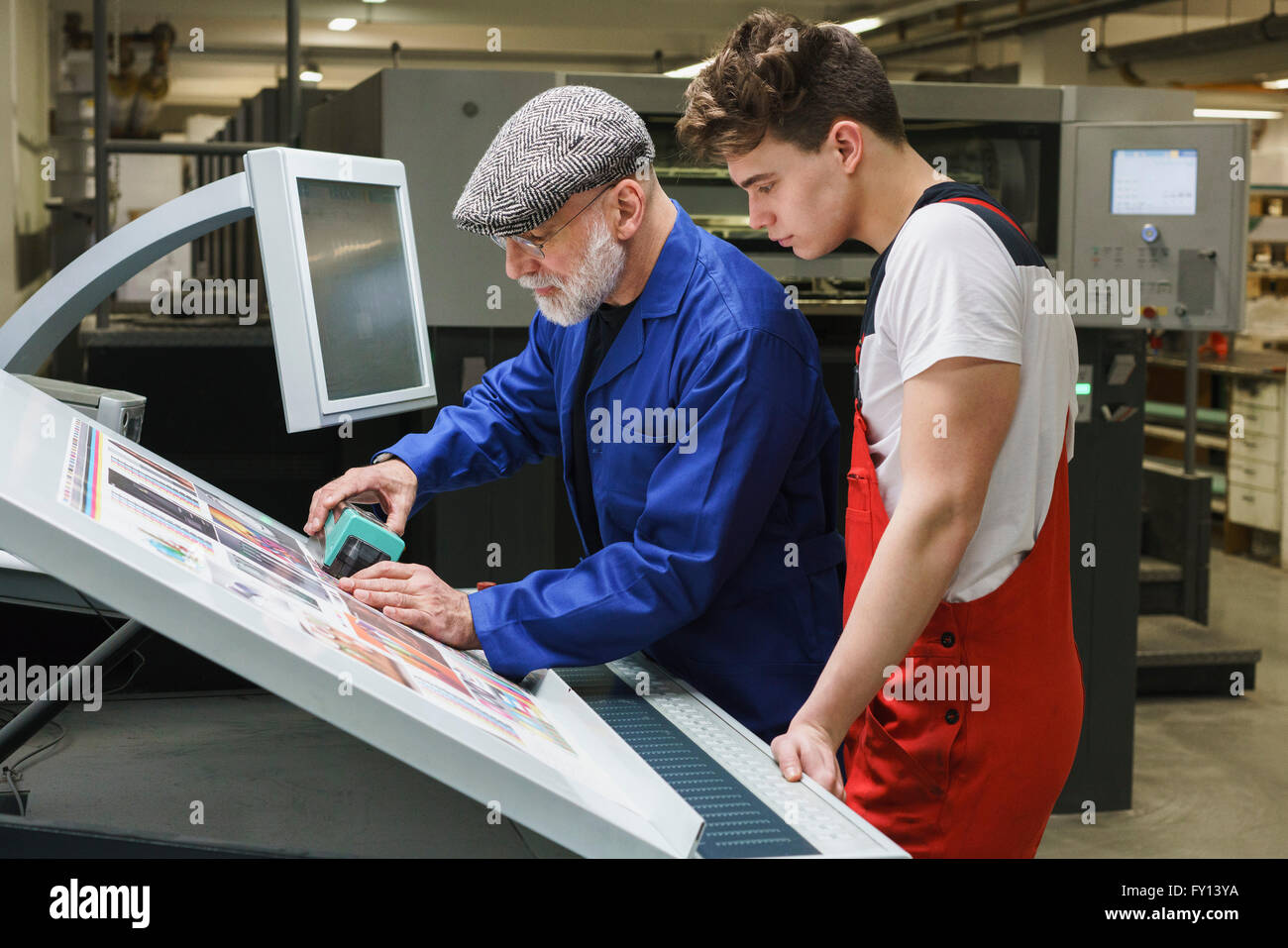 Young worker looking at mature colleague doing quality check of ...