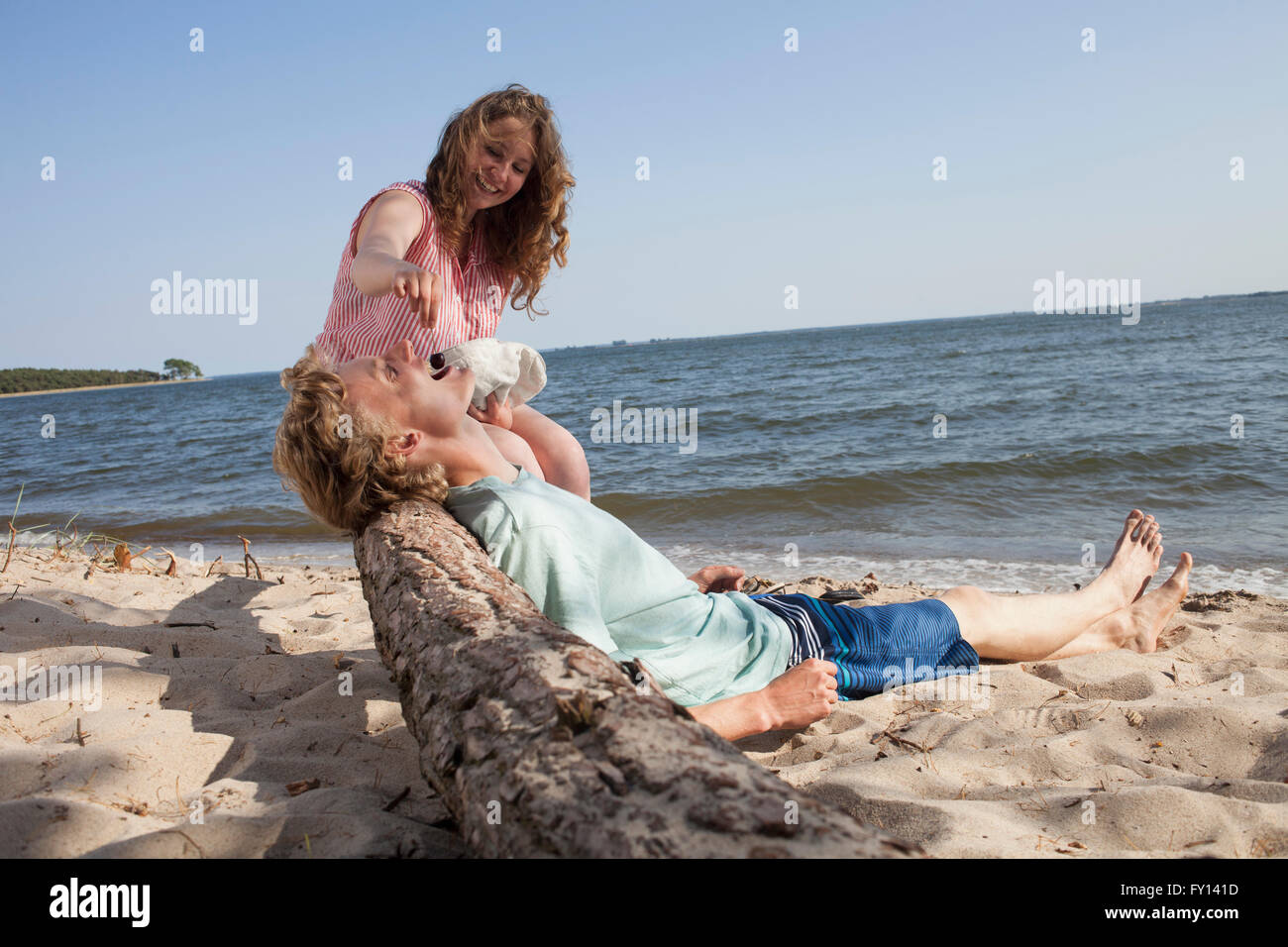 Happy friend feeding cherry to man while relaxing at beach Stock Photo ...
