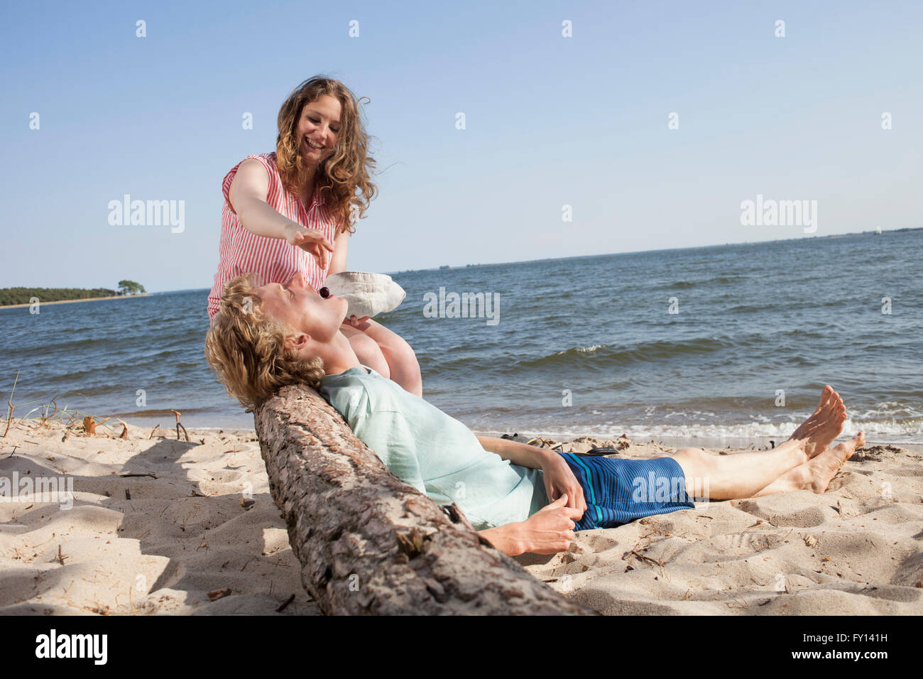 Smiling friend feeding cherry to young man while relaxing at beach ...