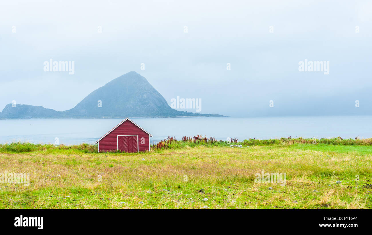 Small red wooden cabin in an open field with sea and big mountain in ...
