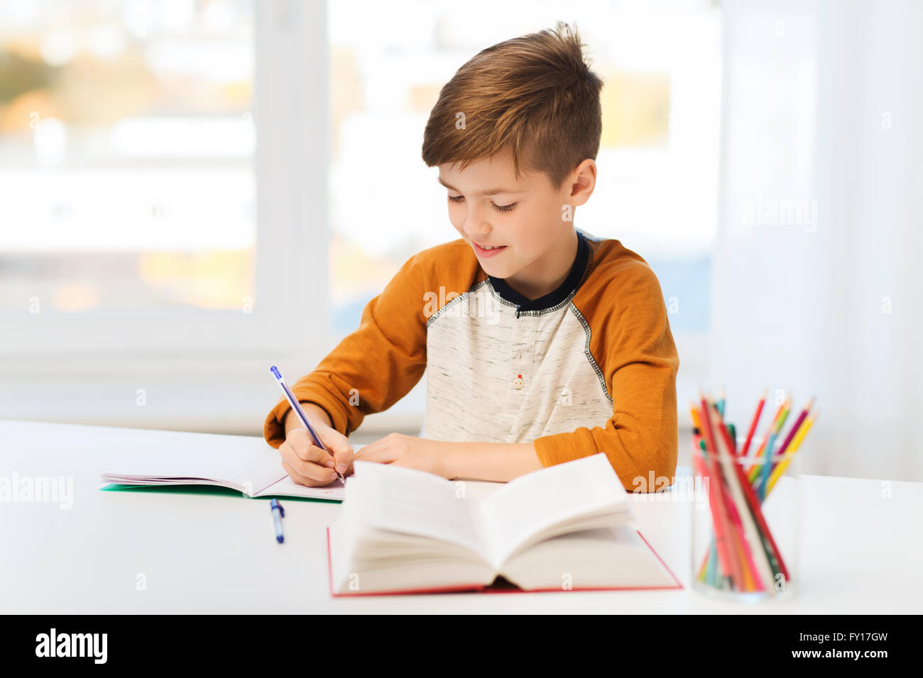 smiling student boy writing to notebook at home Stock Photo - Alamy
