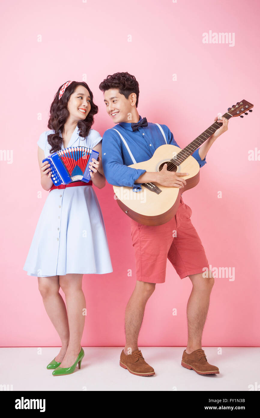 Young smiling couple in retro styles standing back ro back playing ...