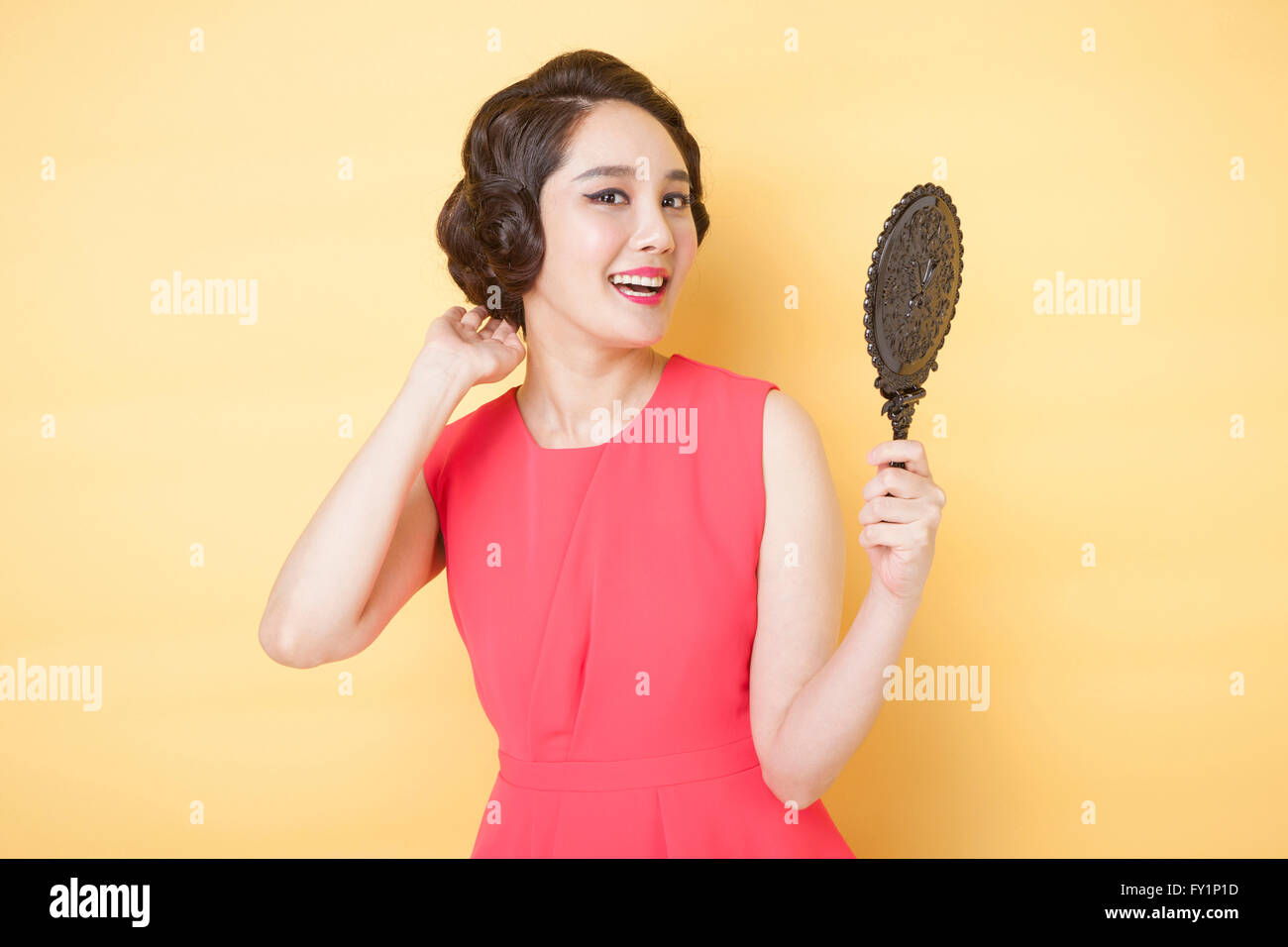 Portrait of young smiling woman in retro style holding a mirror staring ...
