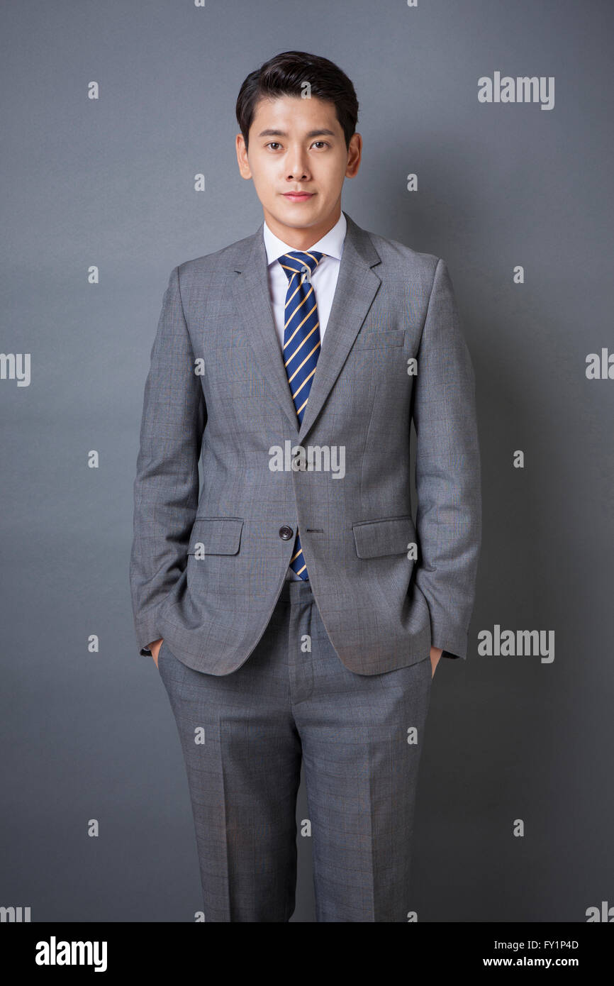 Young smiling business man in gray suit putting hands in pockets ...
