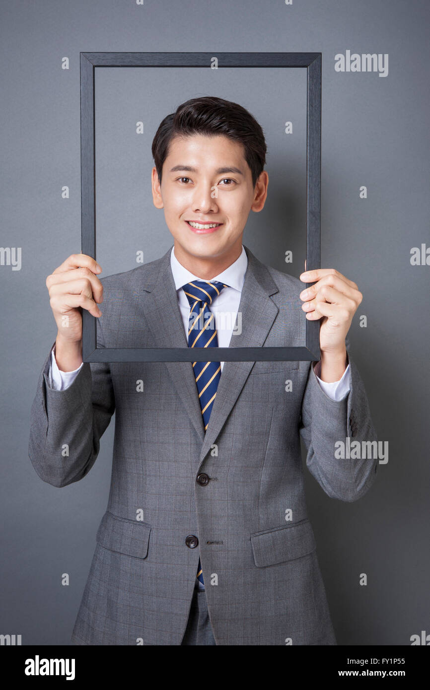 Young smiling business man in gray suit holding a frame staring at ...