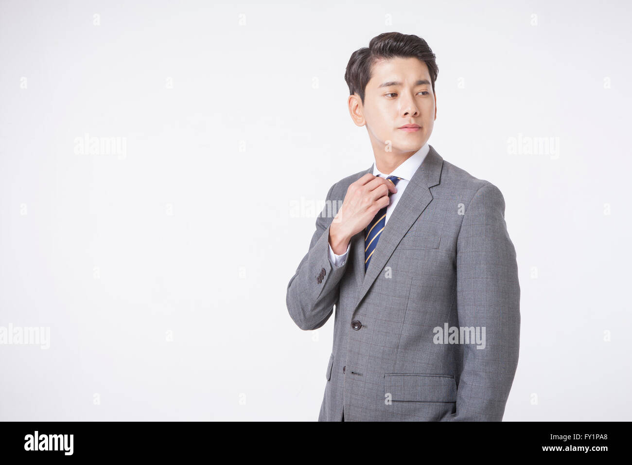 Portrait of young man in gray suit touching his tie looking aside with ...