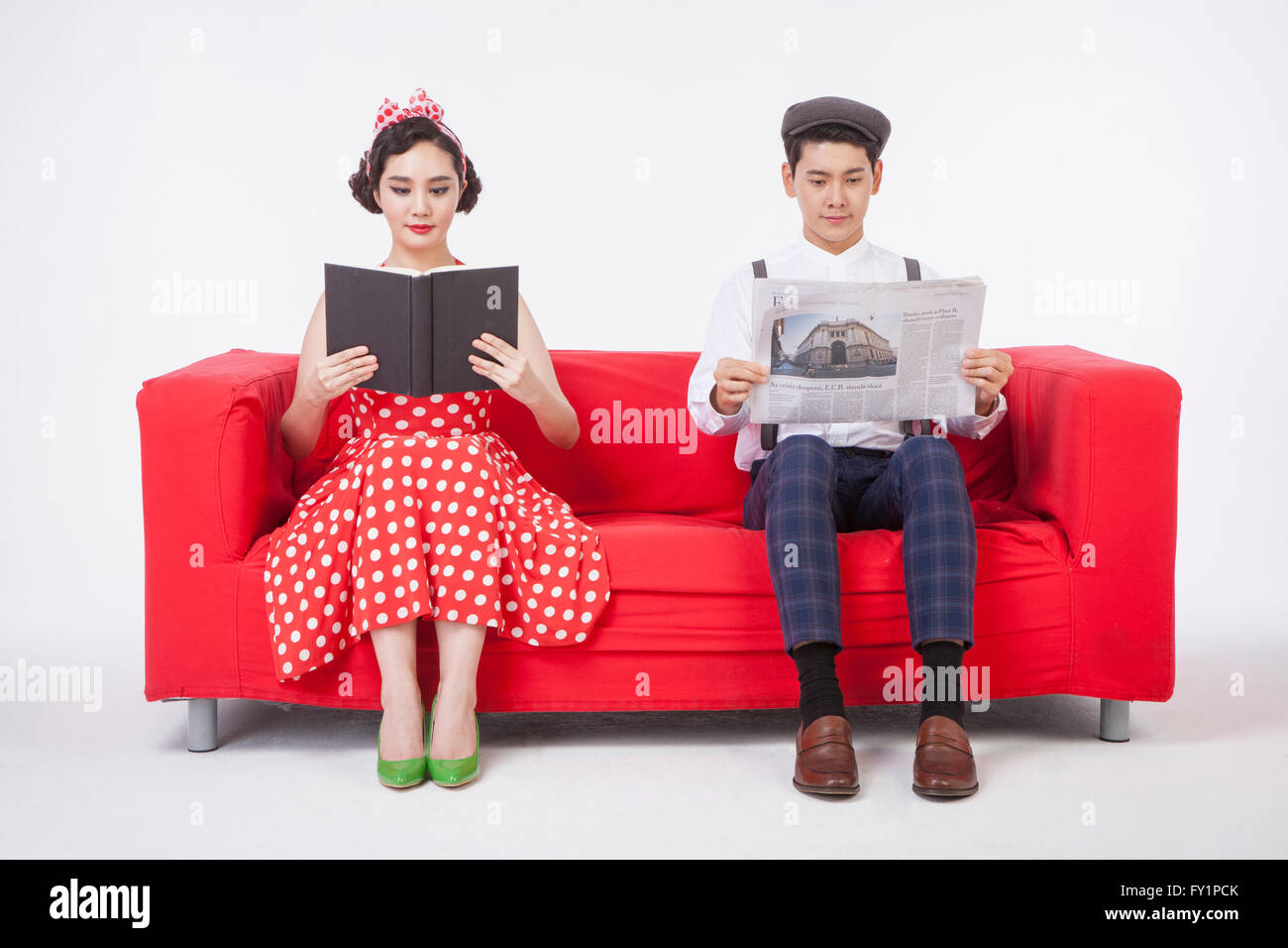 Young couple in retro styles sitting on a sofa side by side reading a ...