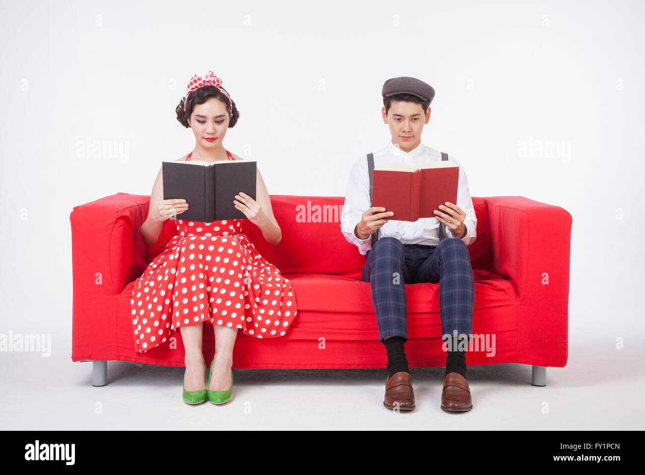 Young couple in retro styles sitting on a sofa side by side reading a ...