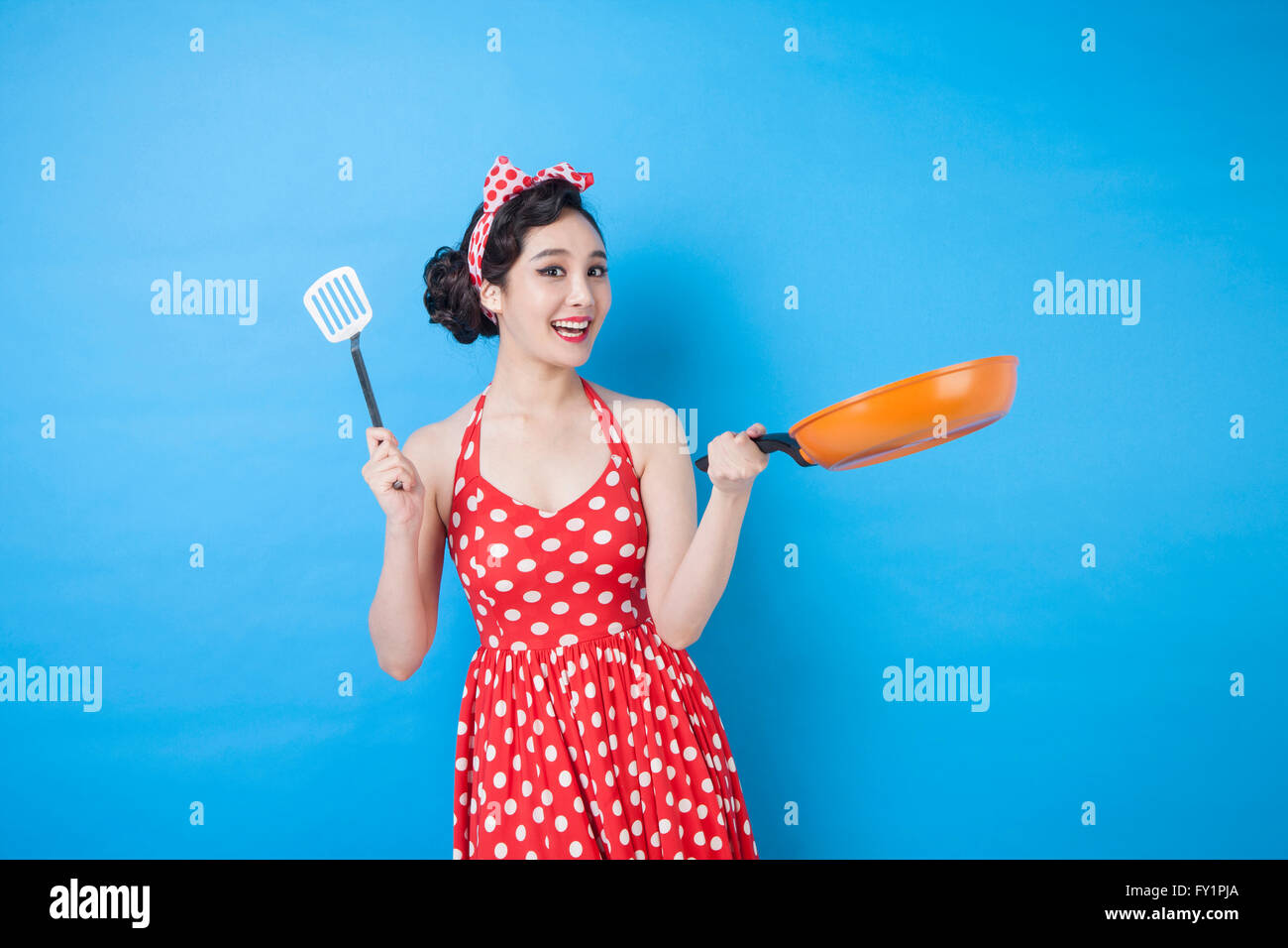 Young smiling woman posing with a spatula and a pan staring at front ...