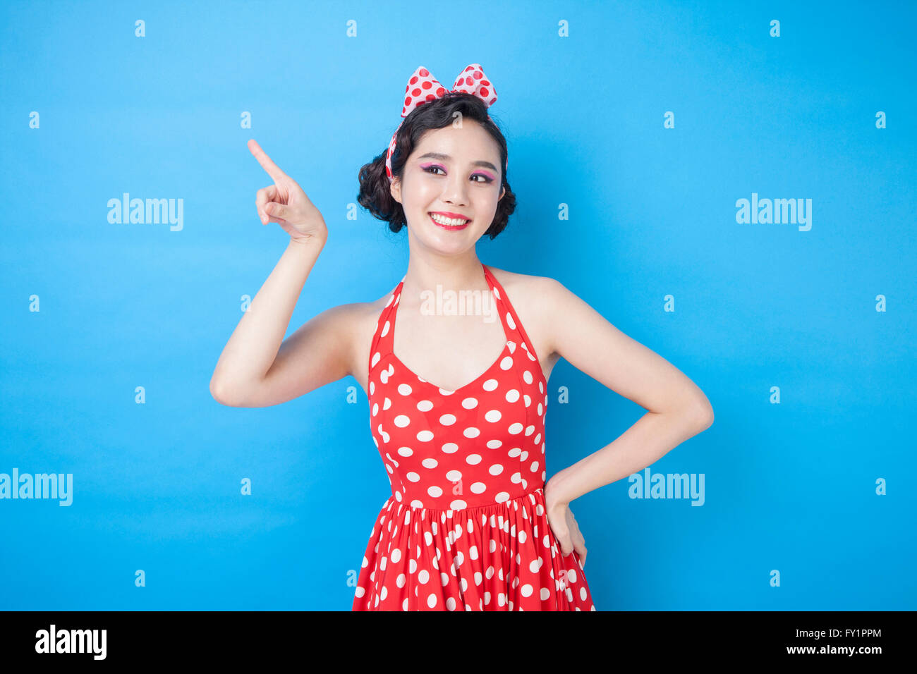 Young smiling woman in retro style posing pointing up with one hand on ...