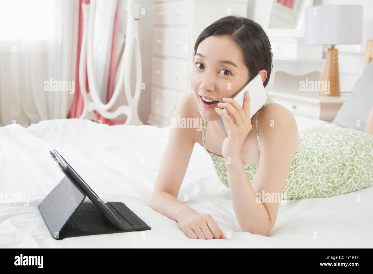 Young smiling woman lying face down on bed talking on the phone staring ...