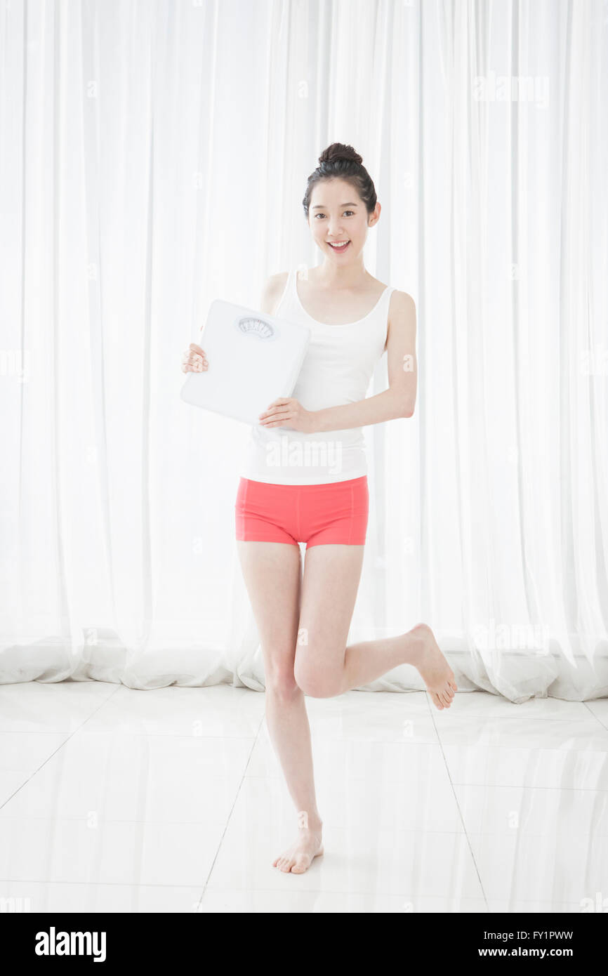 Young smiling woman standing on one foot with a scale Stock Photo - Alamy