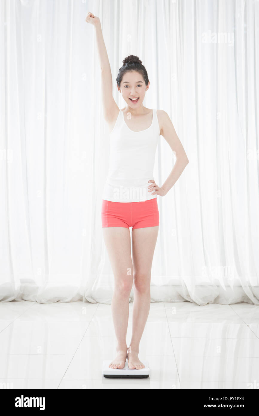 Young smiling woman standing on a scale holding a hand with one hand on ...