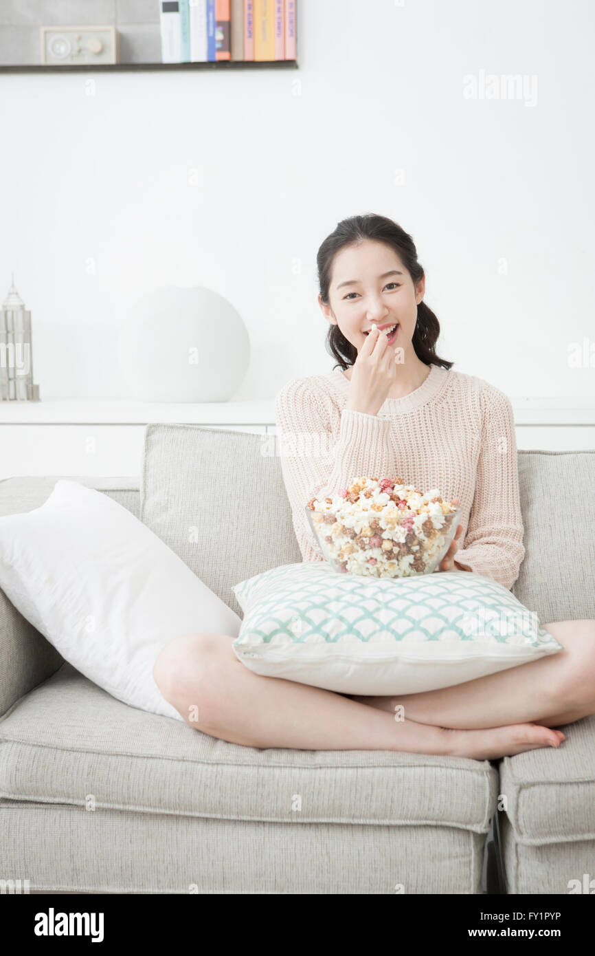 Young smiling woman sitting on sofa eating popcorn Stock Photo - Alamy