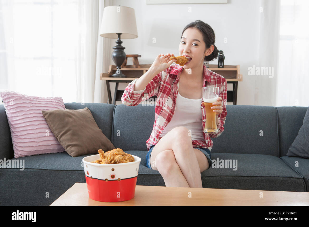 Young smiling woman sitting on sofa having fried chicken and beer Stock ...