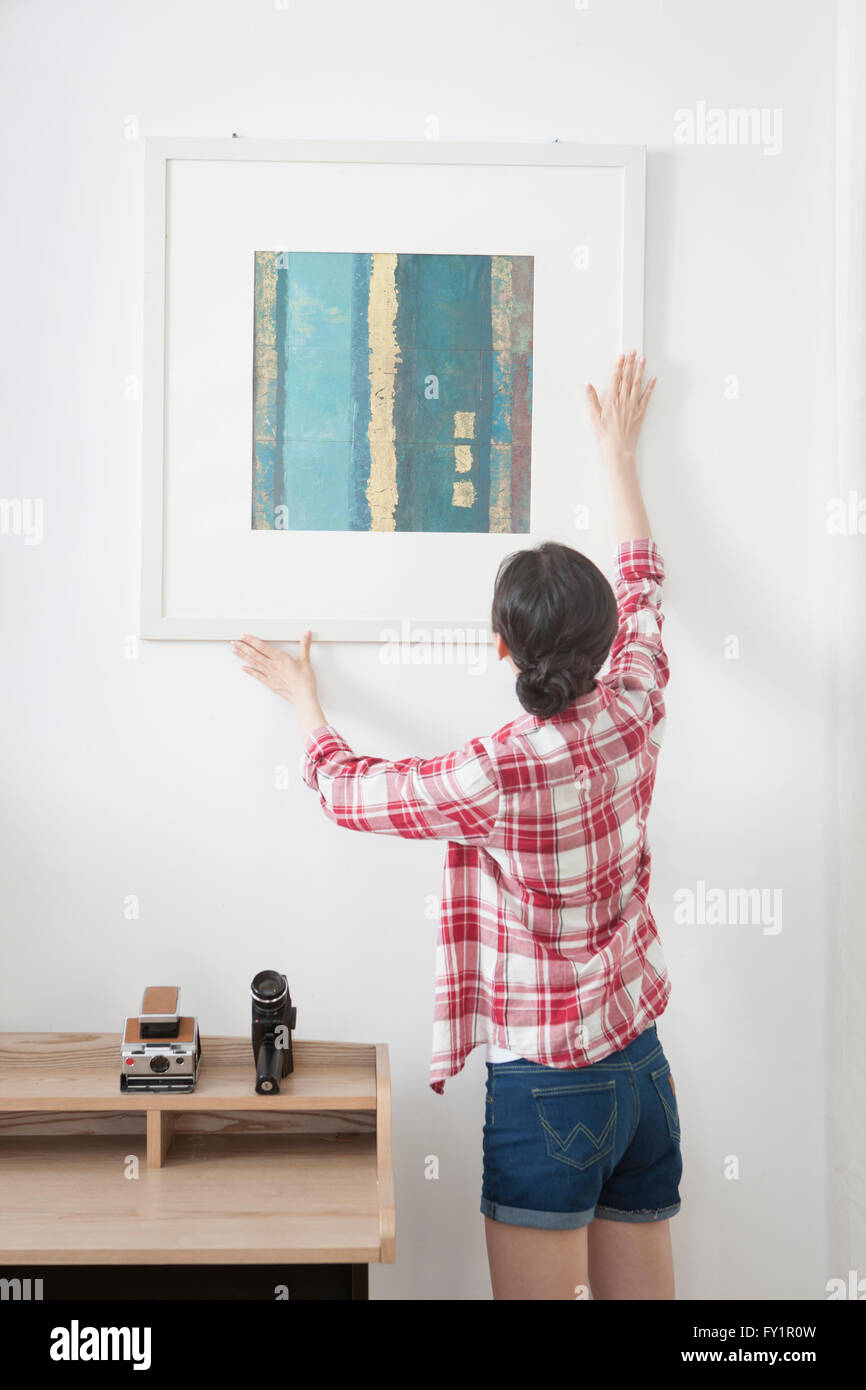 Back of young woman hanging a picture frame on the wall looking up ...
