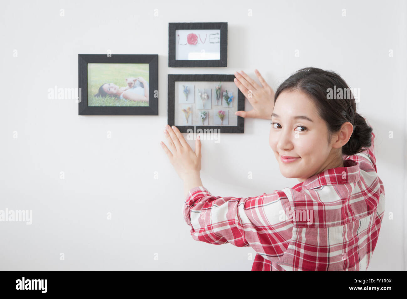 Side view portrait of young smiling woman hanging pictures on the wall ...