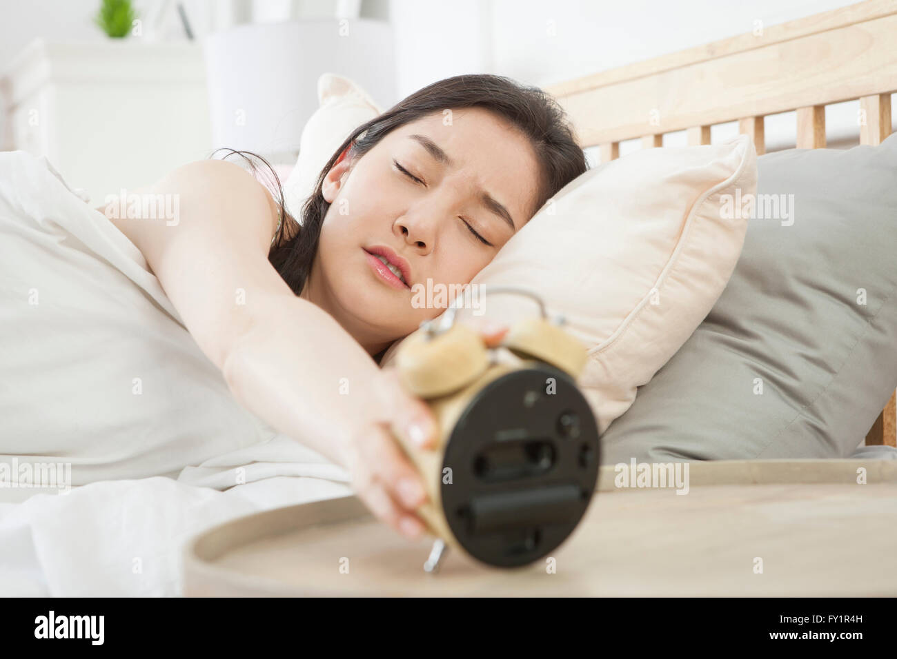 Portrait Of Young Woman Lying Down In Bed Turning Off Alarm Clock With