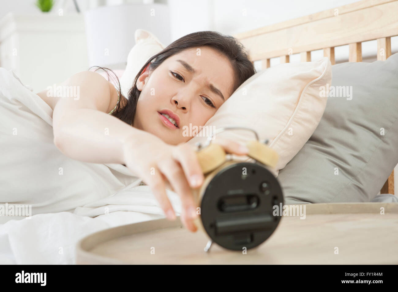 Portrait of young woman with a frown on her face lying down in bed ...