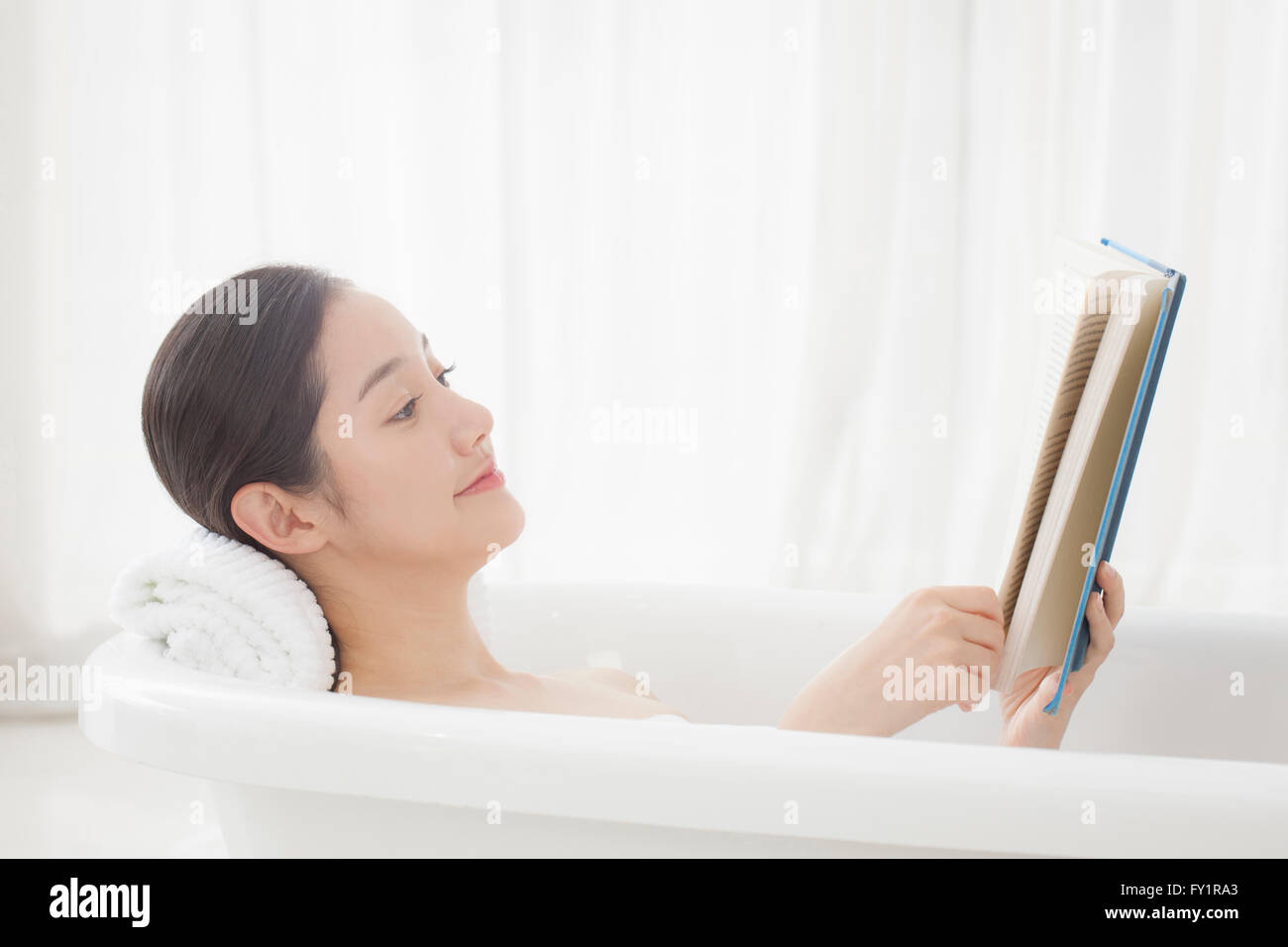Side view portrait of young woman resting and reading a book in a tub ...