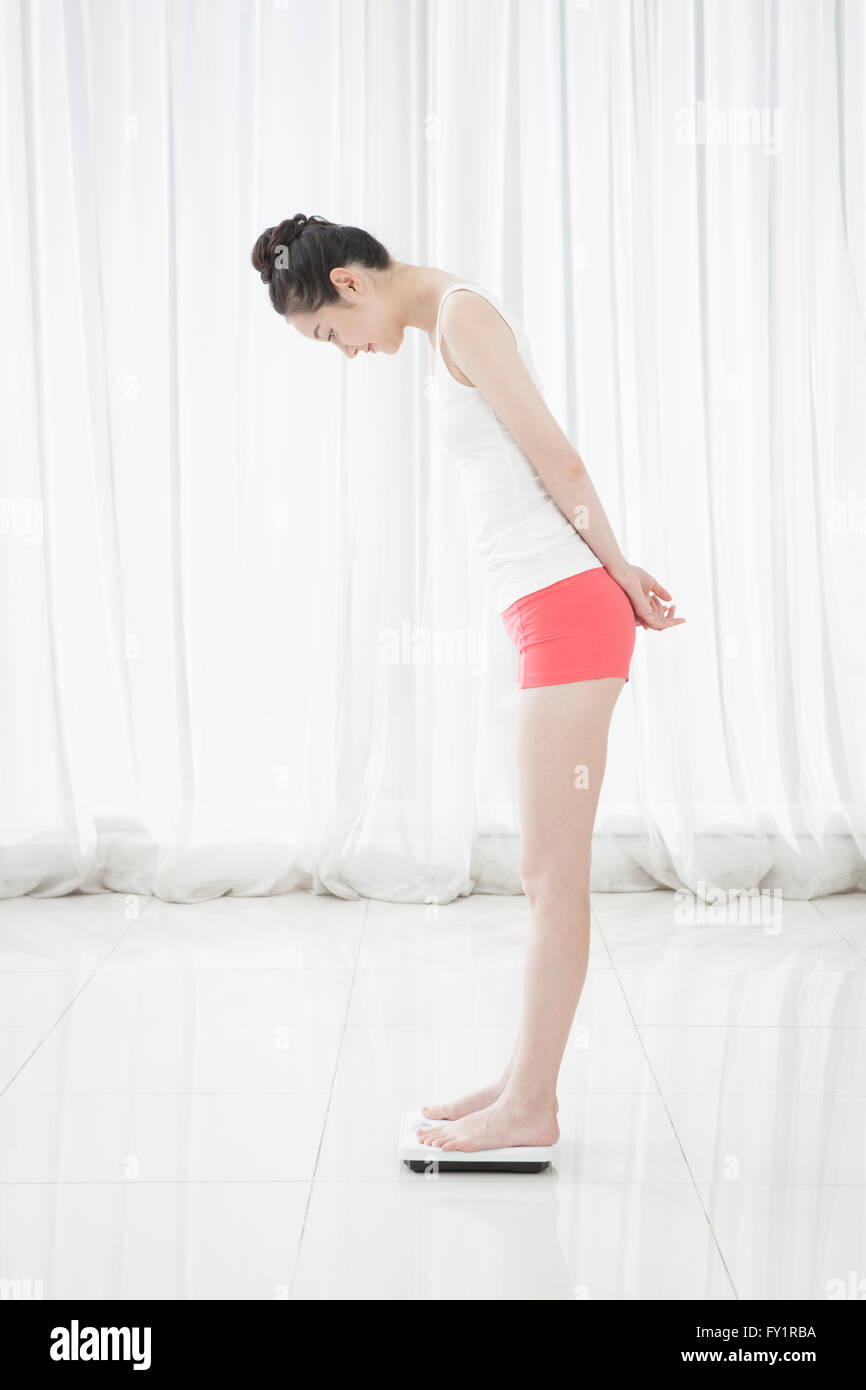 Side view of young woman standing on a scale looking down Stock Photo ...