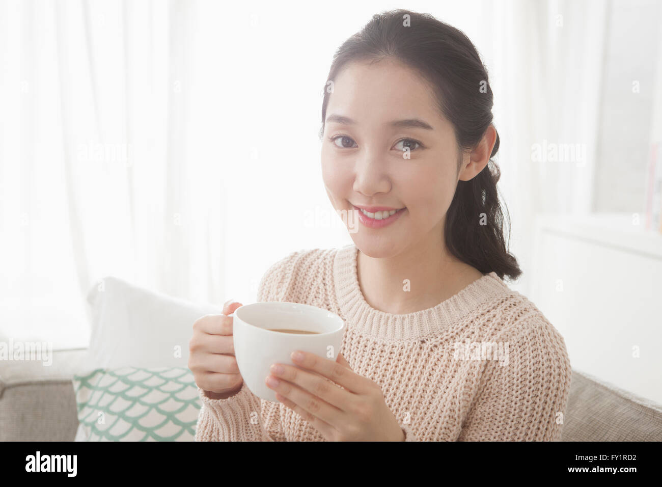 Portrait of young smiling woman holding a cup of tea staring at front ...