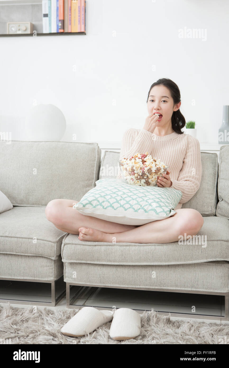 Young woman sitting on sofa eating popcorn Stock Photo - Alamy