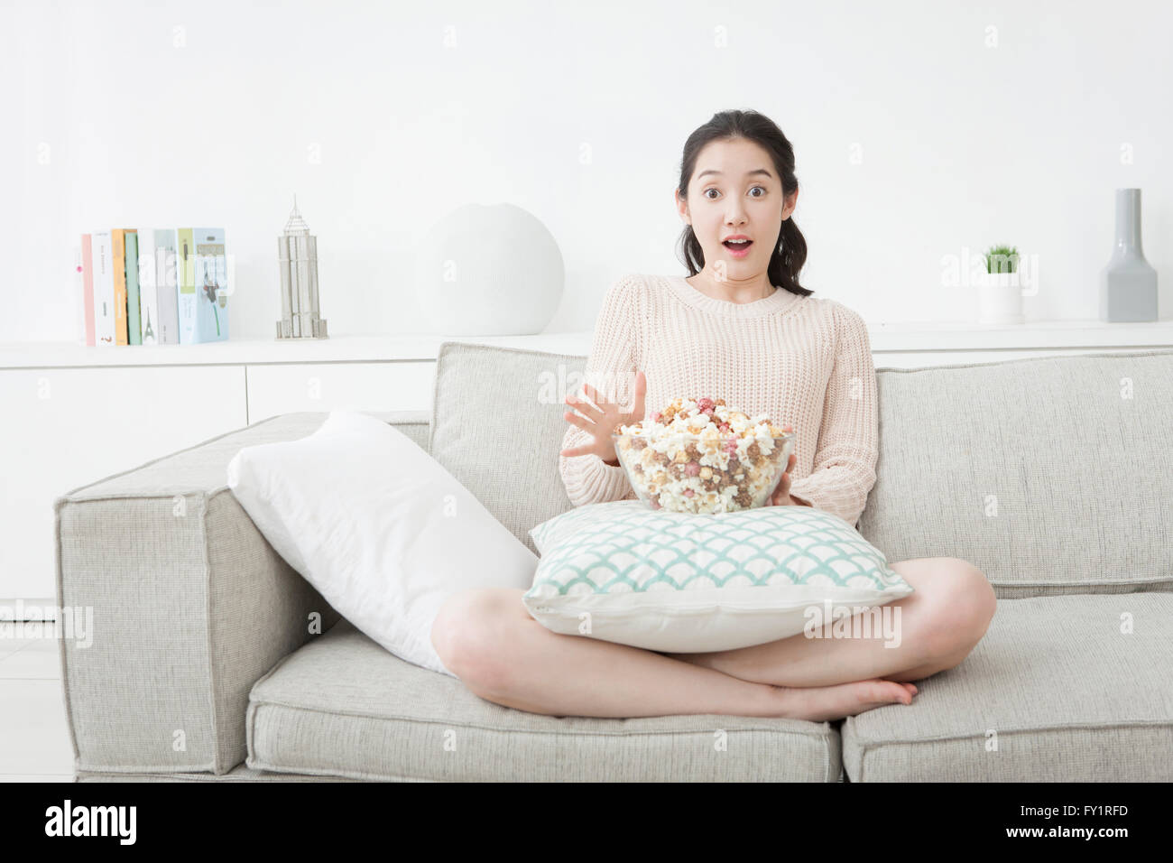 Young woman sitting on sofa eating popcorn with a surprised face Stock ...