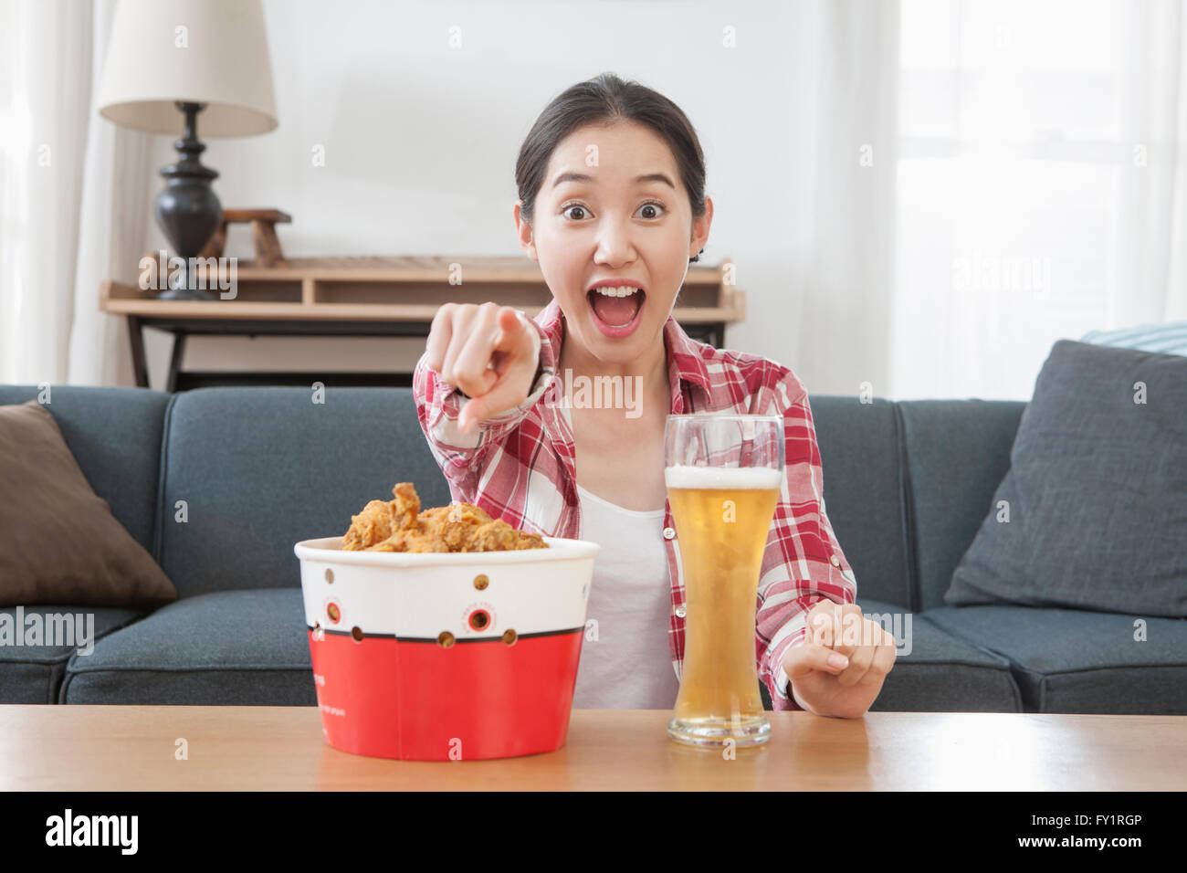Portrait of young smiling woman pointing to front with chicken and beer ...