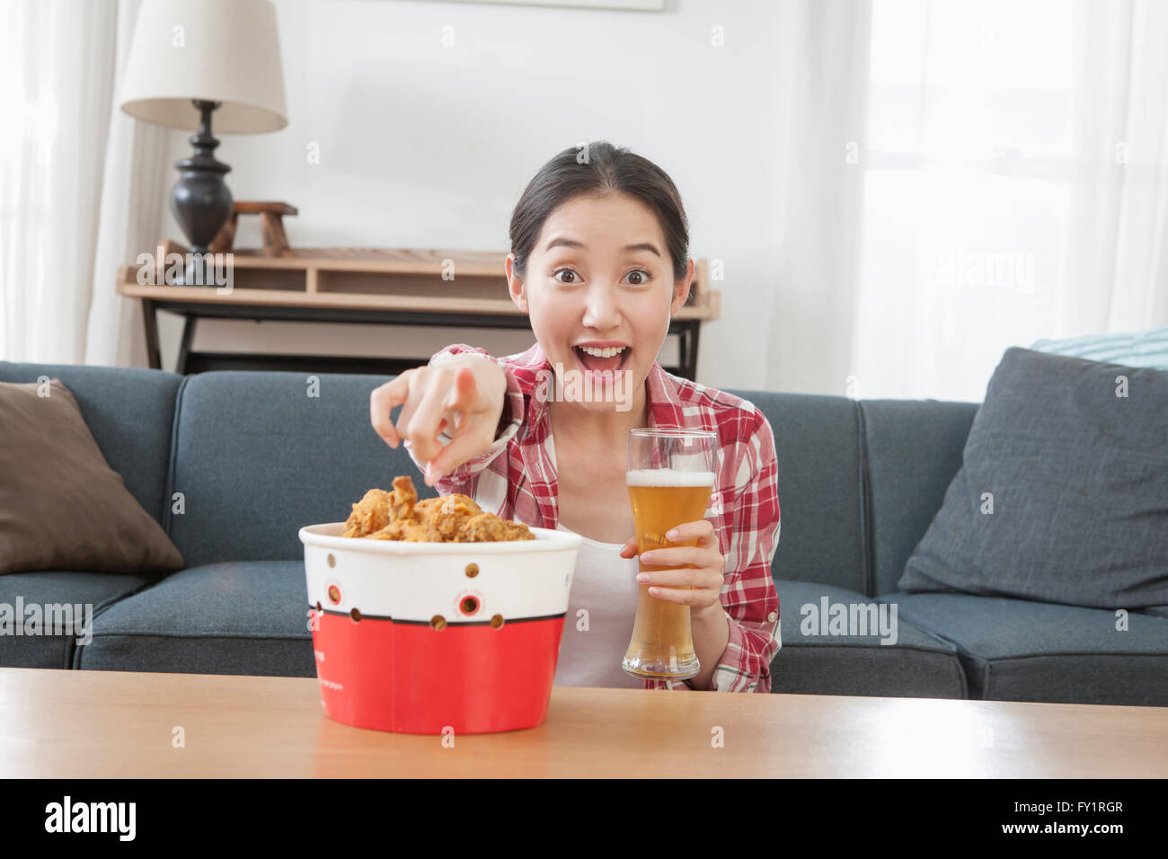 Portrait of young smiling woman pointing to front with chicken and beer ...
