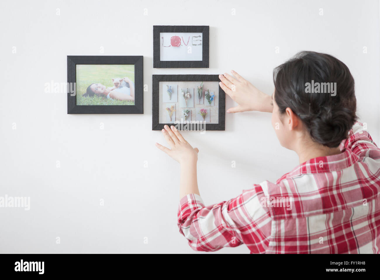 Back of young woman decorating wall with small frames Stock Photo - Alamy