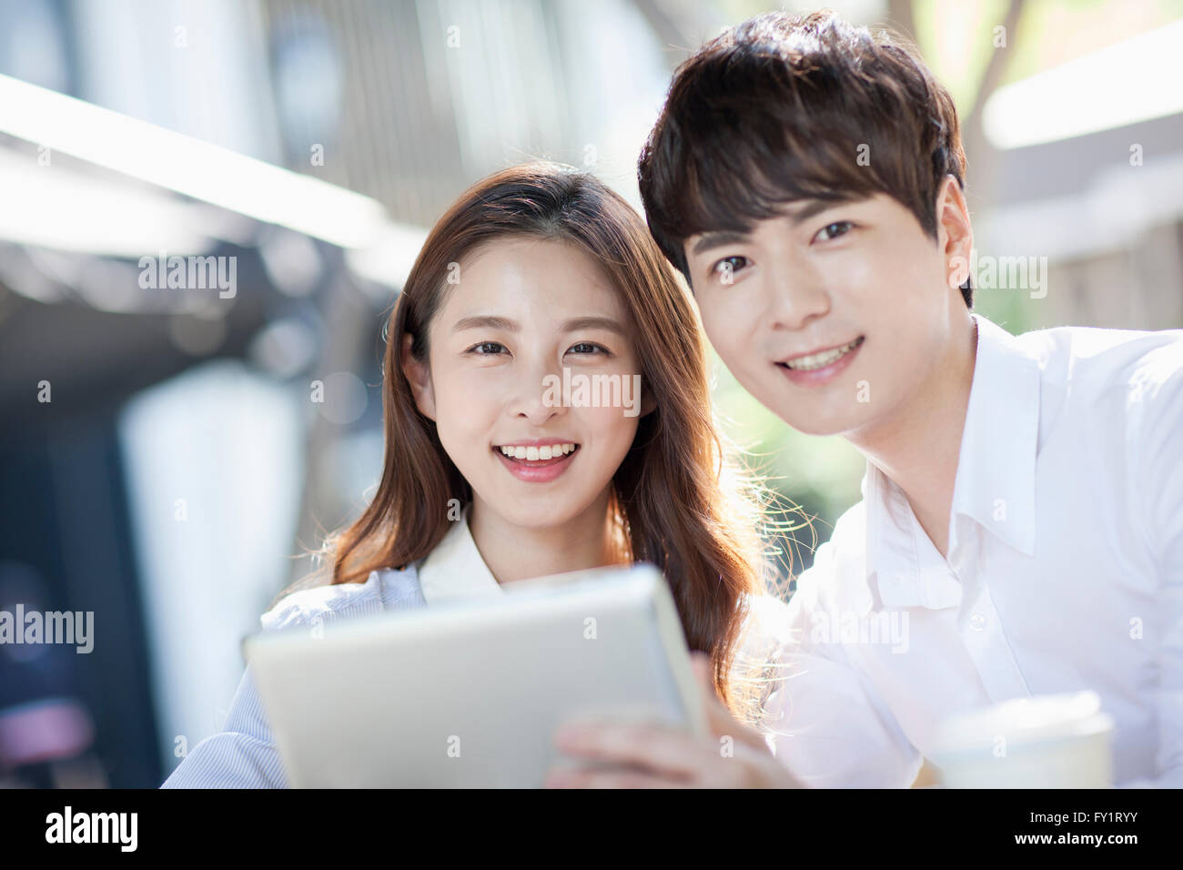 Portrait of young smiling couple sharing a tablet staring at front ...