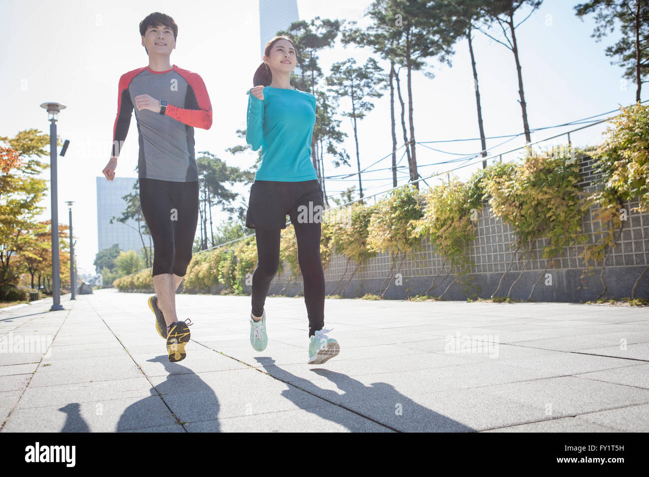 Low angle view of young smiling couple jogging at park Stock Photo - Alamy