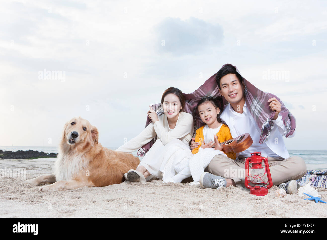 Family covering up themselves with a blanket all seated on the sandy ...