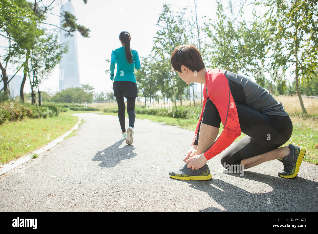 Back appearance of a jogging woman and a man tying his shoelace at the ...