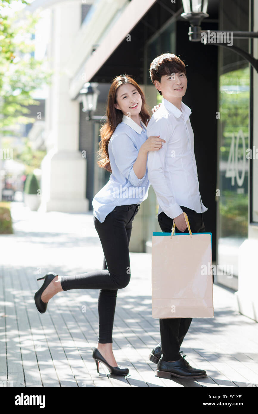 Woman standing on one foot behind her boy friend holding shopping bags ...