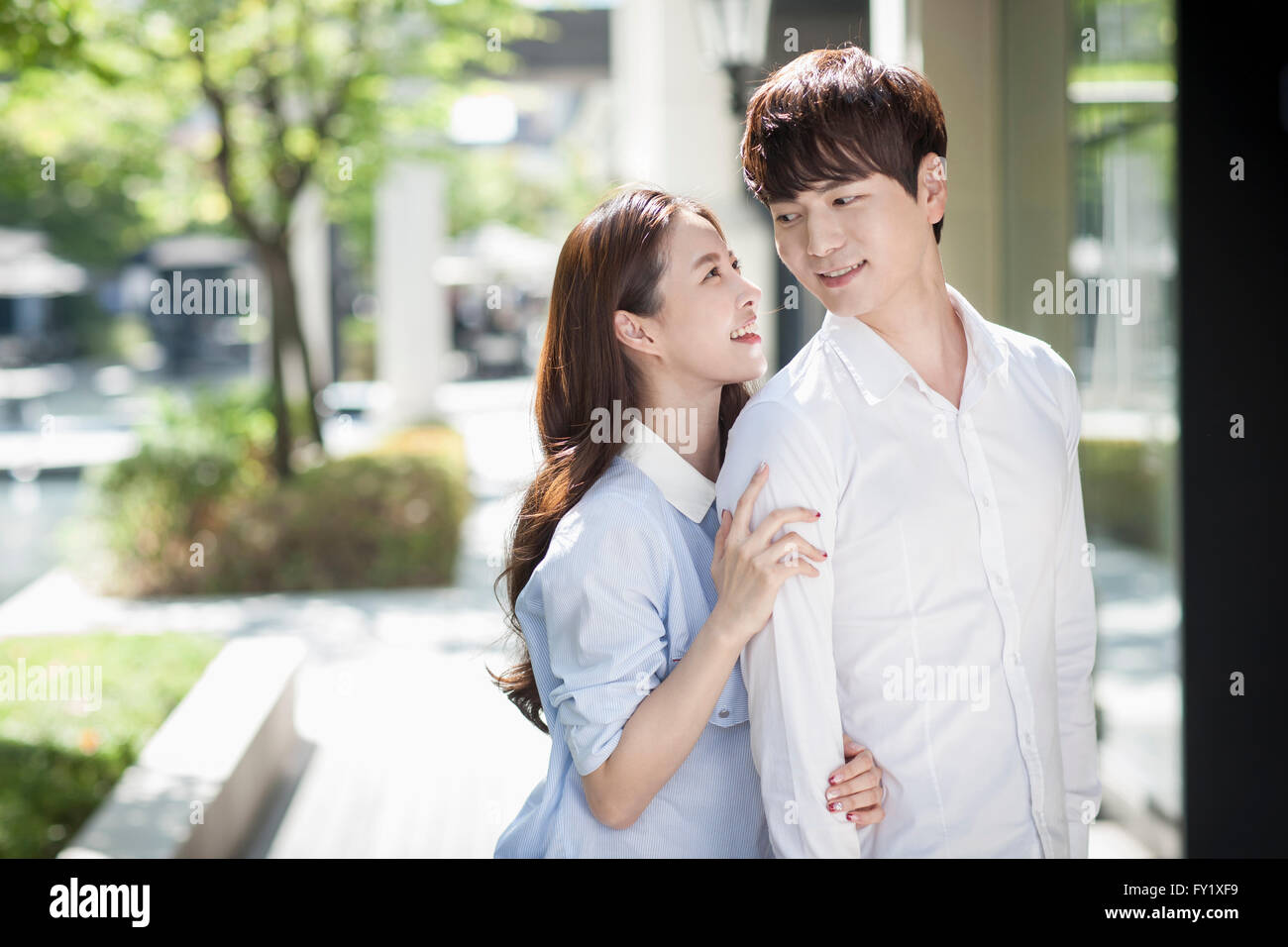 Woman leaning on her boyfriend's back outside both looking at each ...