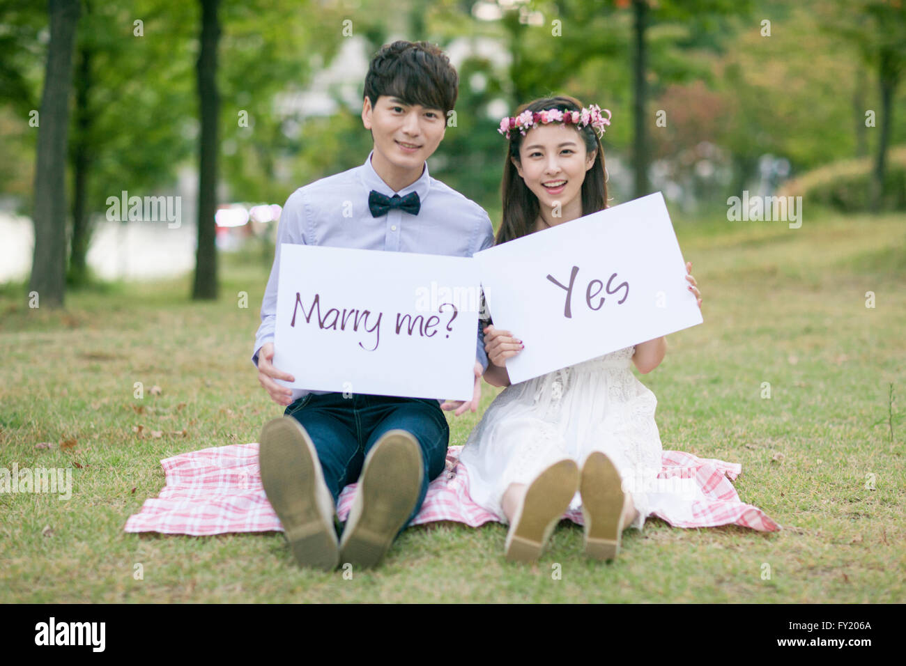Bride and groom holding a message of marry me and yes both seated on a ...