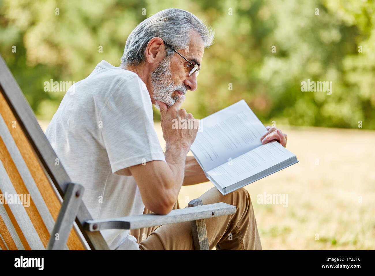 Old man reading a book on a deck chair in the park in summer Stock ...