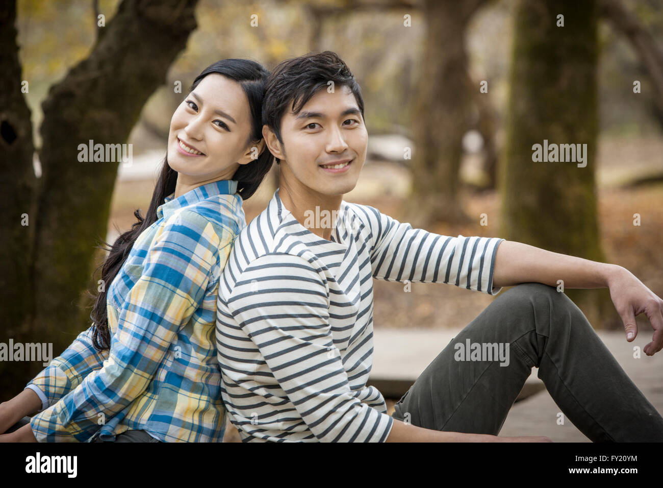 Couple seated back to back each other and smiling outside Stock Photo ...