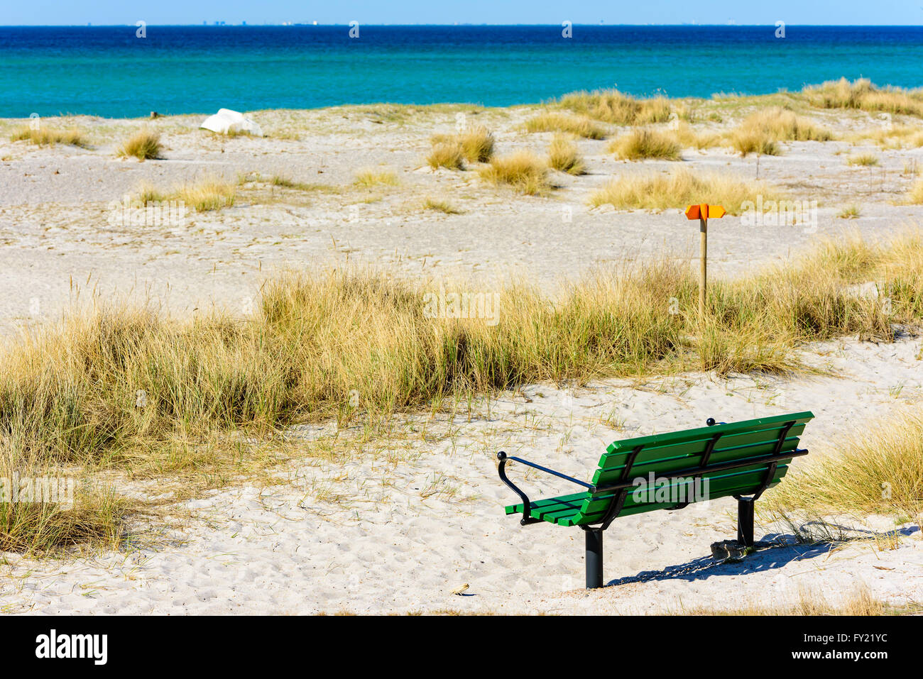 Green wooden bench overlooking the sandy beach with a boat upside down ...