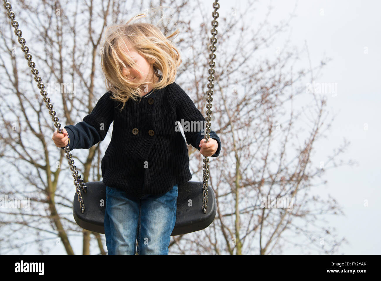 Little child blond girl having fun on a swing outdoor. Summer playground. Girl swinging high ...