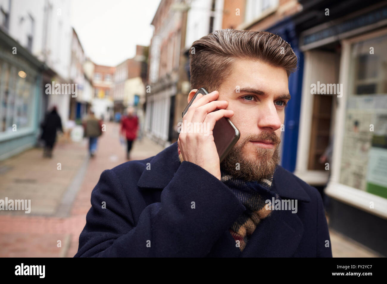 Young Man Walking Down Urban Street Using Mobile Phone Stock Photo - Alamy
