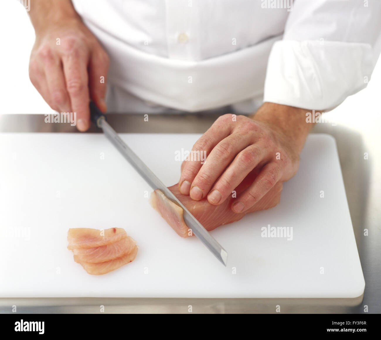 Cutting thin slices from a block of raw yellowtail tuna (hamachi Stock ...
