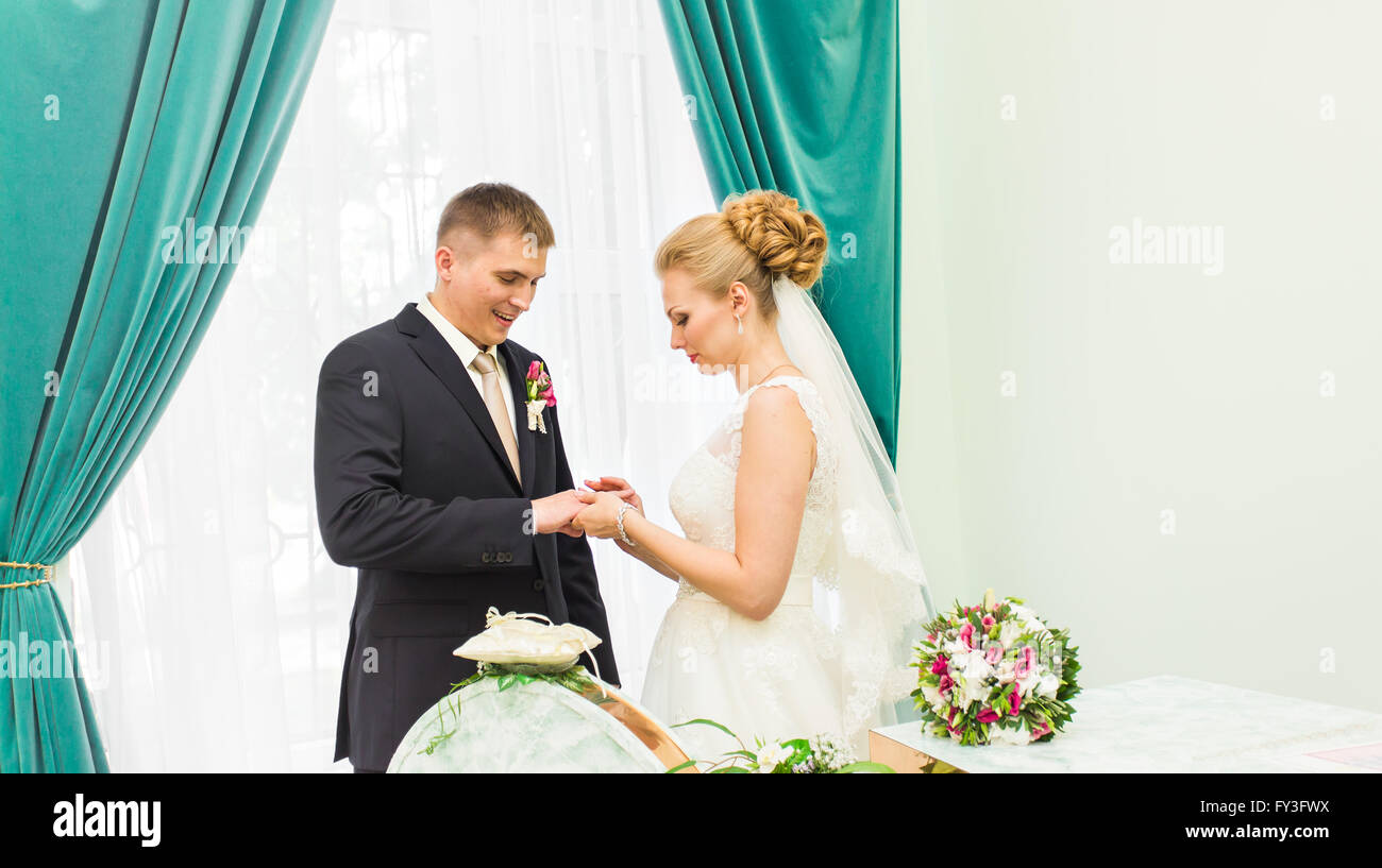 Bride slipping ring on finger of groom at wedding Stock Photo - Alamy