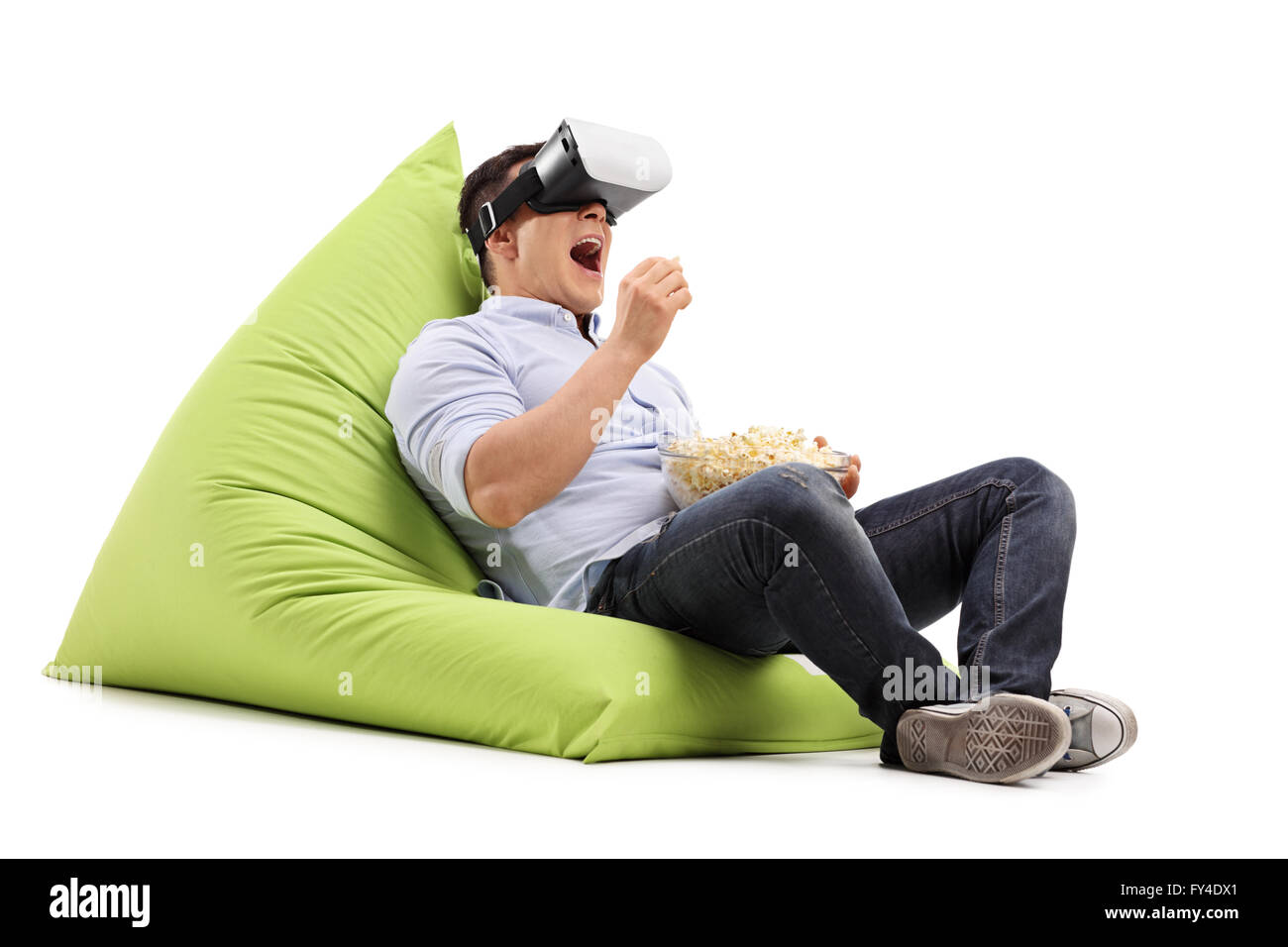 Young man eating popcorn and watching something on a VR goggles seated ...