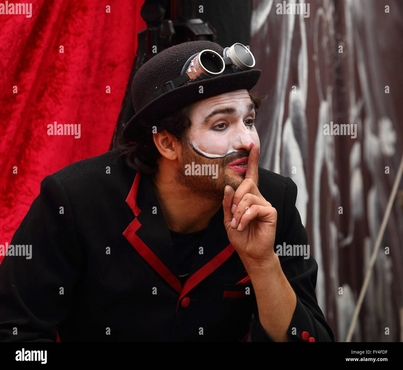 Male clown with bowler hat and goggles with one finger to his lips in a ...